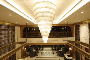 Um hall com um lustre grande, área de estar e uma escadaria.