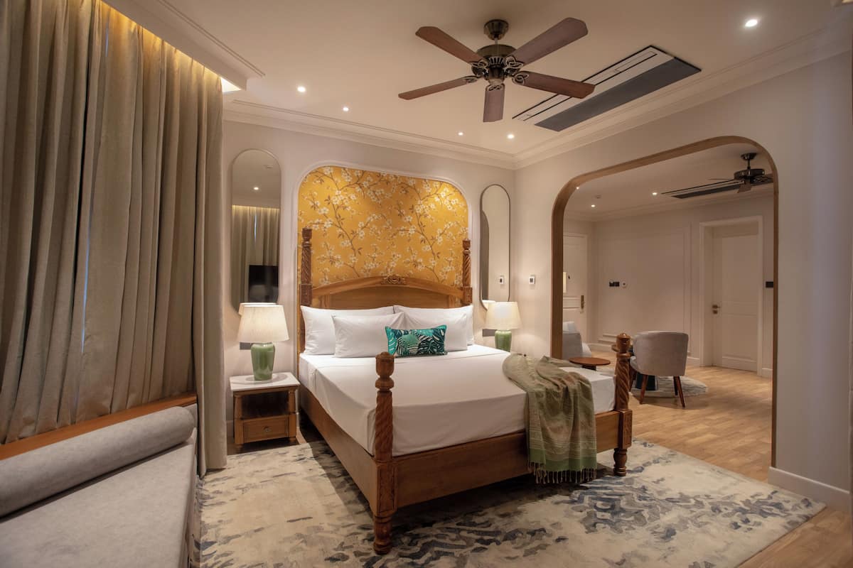 Quarto com cama de dossel, duas mesinhas de cabeceira, um criado-mudo, uma cadeira e um ventilador de teto.