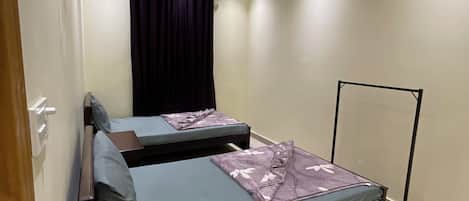 Quarto com duas camas de solteiro, ventilador de teto e janela com cortinas.