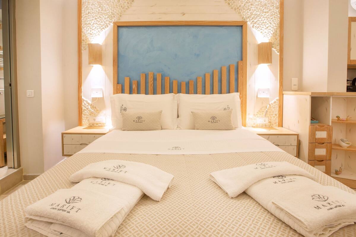 Quarto de hotel bem arrumado com uma cama grande, duas mesas de cabeceira com abajures, uma cabeceira de madeira e uma parede azul.