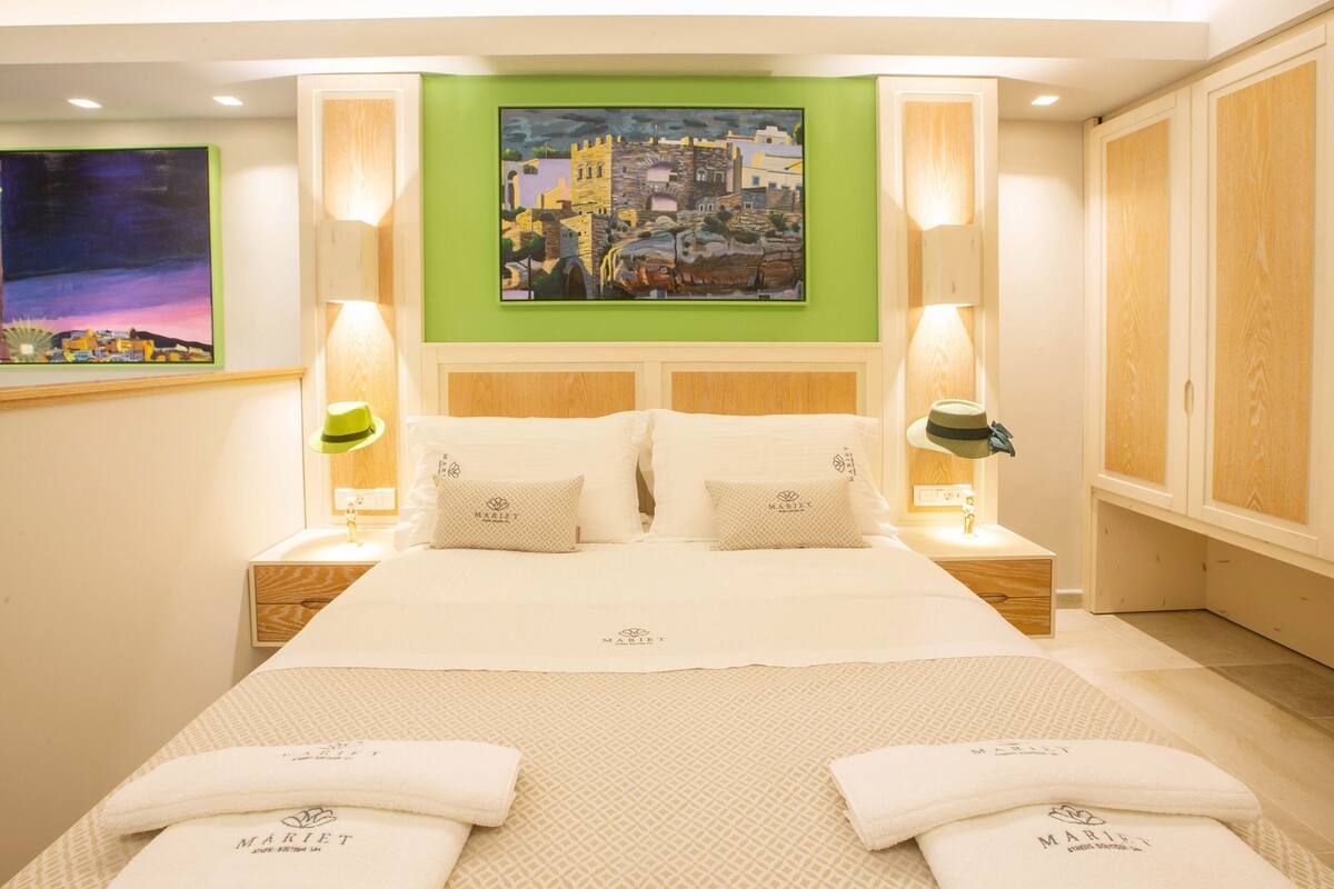 Quarto bem arrumado com uma cama grande, duas luminárias de cabeceira, uma parede verde e um quadro sobre a cama.