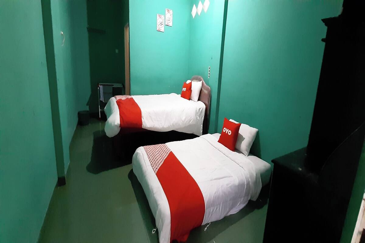 Duas camas de solteiro com roupa de cama vermelha e branca em quarto com paredes verde-água.