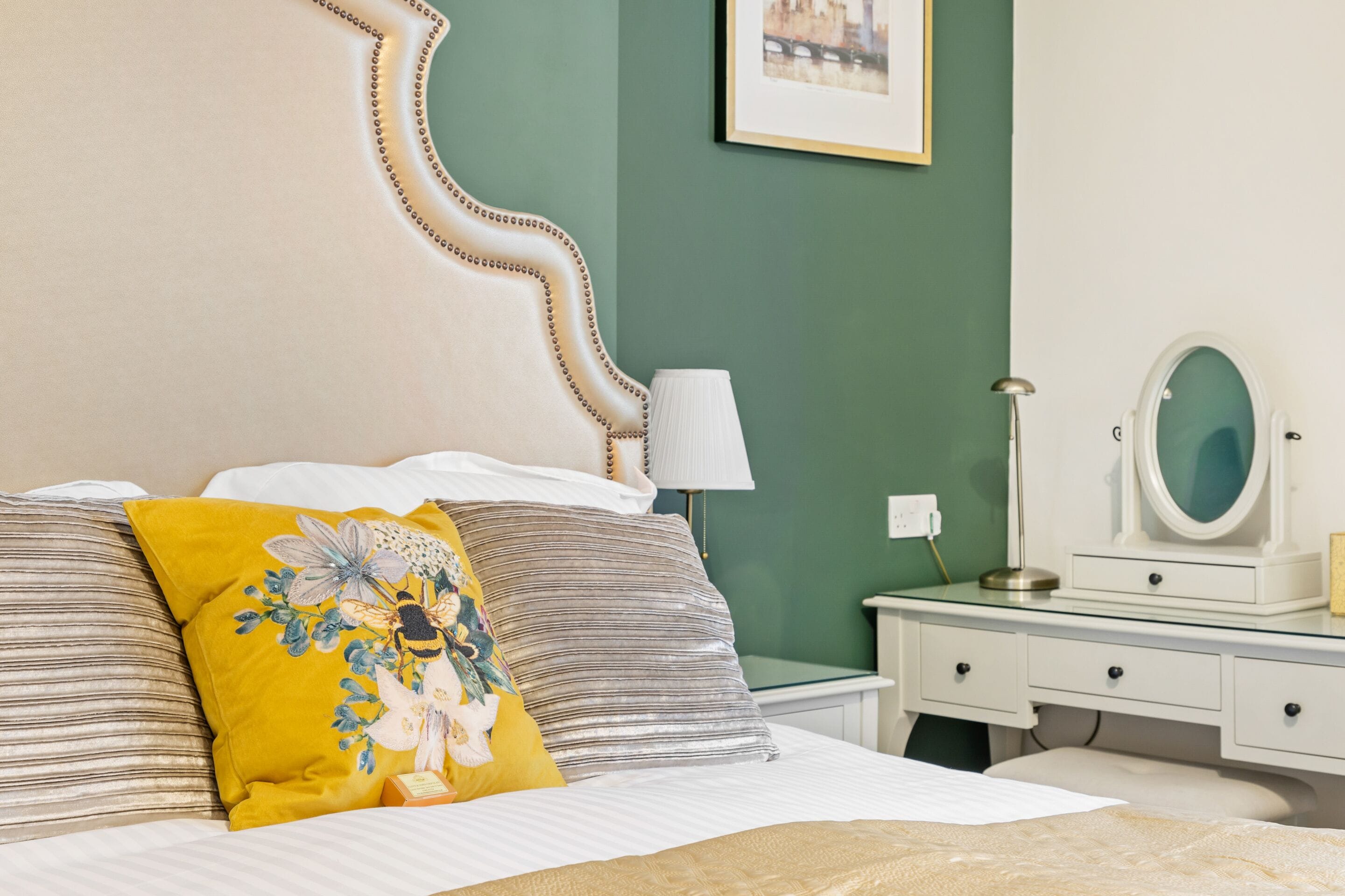 Cama bem arrumada com travesseiro estampado, abajur e cômoda com espelho.
