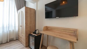 Quarto com guarda-roupa de madeira, uma pequena geladeira preta, escrivaninha de madeira e televisão de tela plana fixada na parede.