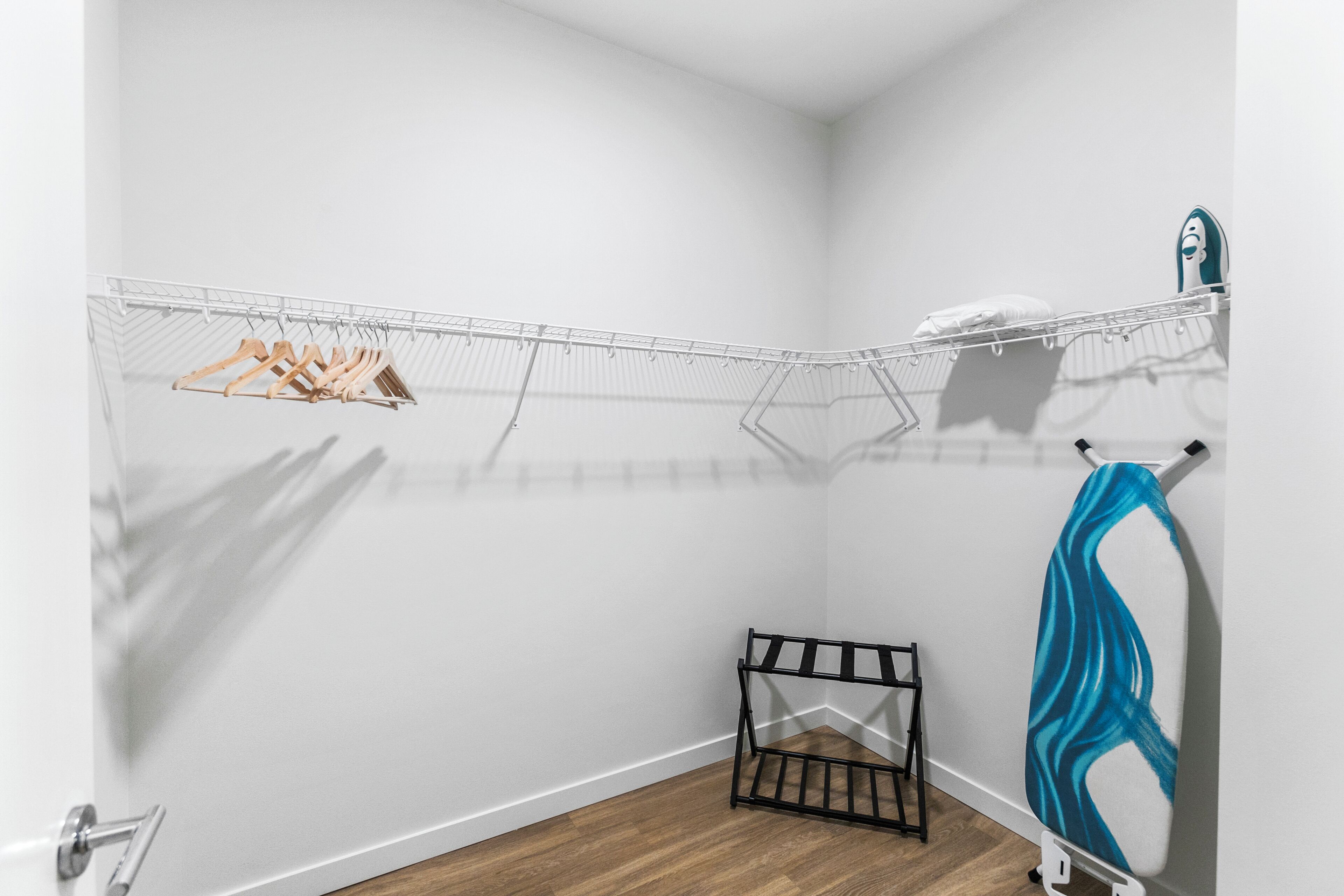 Canto de um quarto com parede branca, assoalho de madeira, varal de metal e toalha azul.