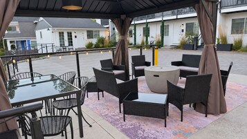 Uma área externa com mesas e cadeiras, uma mesa redonda e um espaço coberto com cortinas.