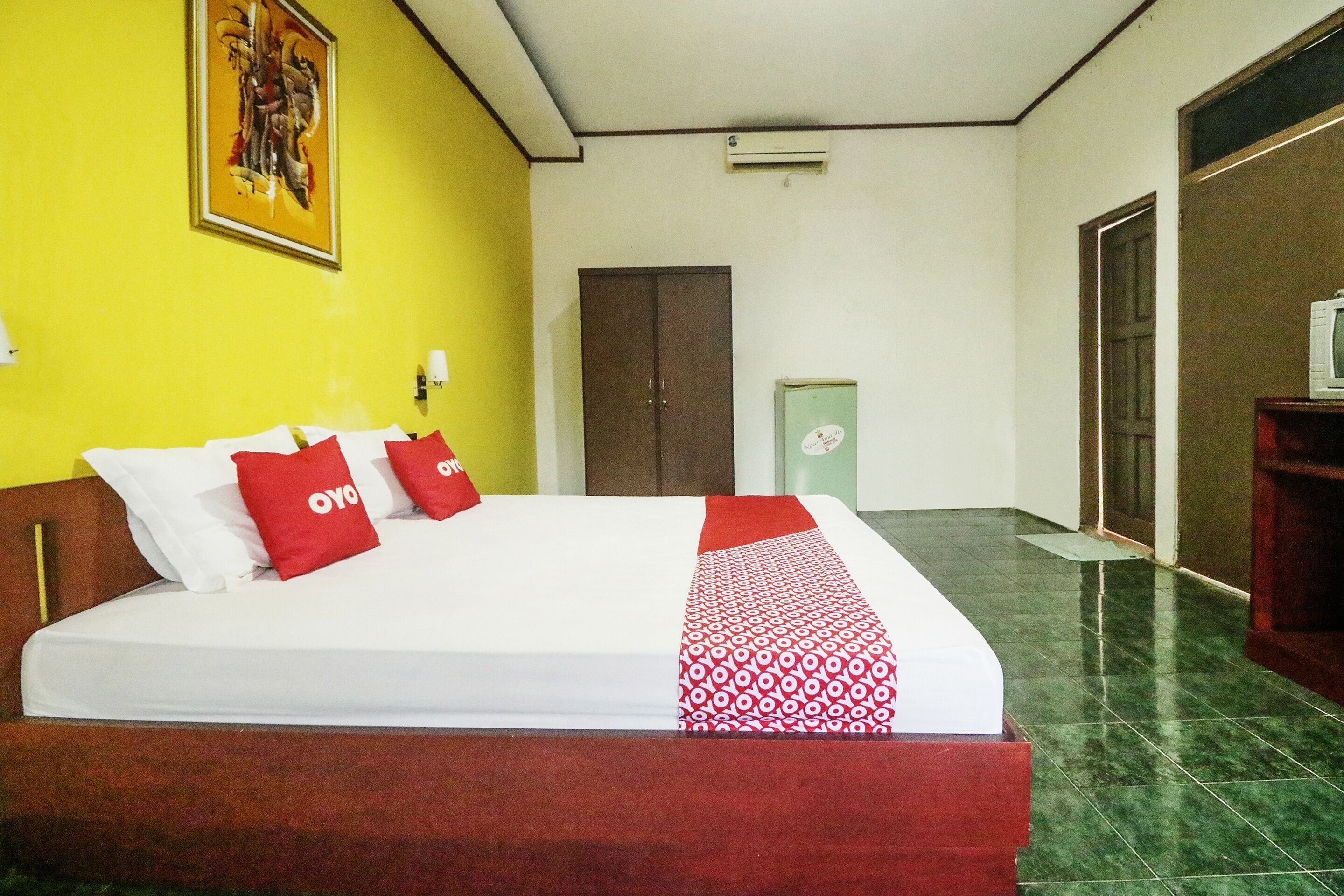 Quarto de hotel com cama, guarda-roupa, televisão e um quadro na parede.