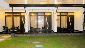 Entrada moderna de hotel com área de estar coberta ao ar livre, gramado bem cuidado e uma porta grande e decorativa.