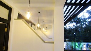 Uma escadaria com luminárias pendentes, uma porta e vista para um jardim com plantas e uma cerca.