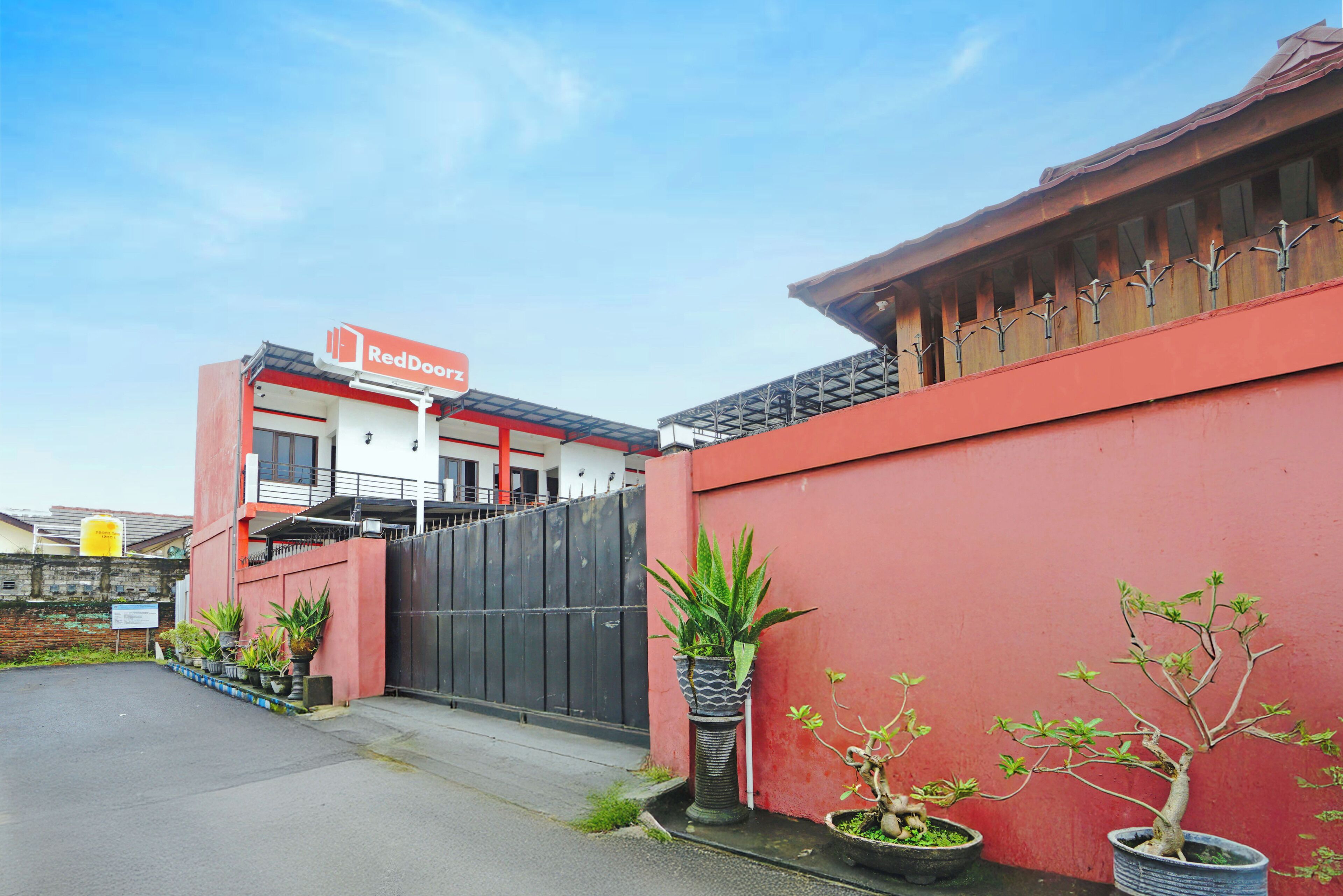 Um edifício RedDoorz com entrada gradeada, plantas em vasos e uma parede vermelha.