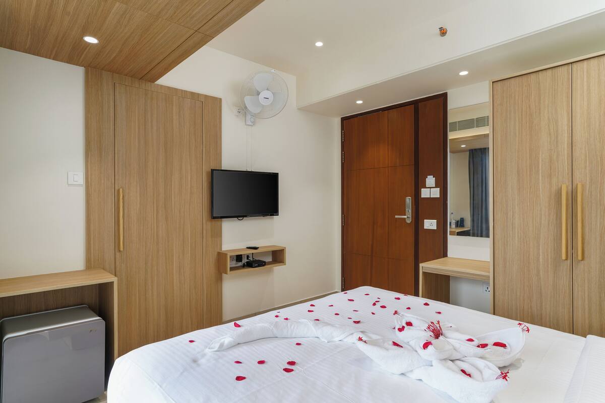 Quarto de hotel com cama, guarda-roupa de madeira, televisão e uma pequena escrivaninha.