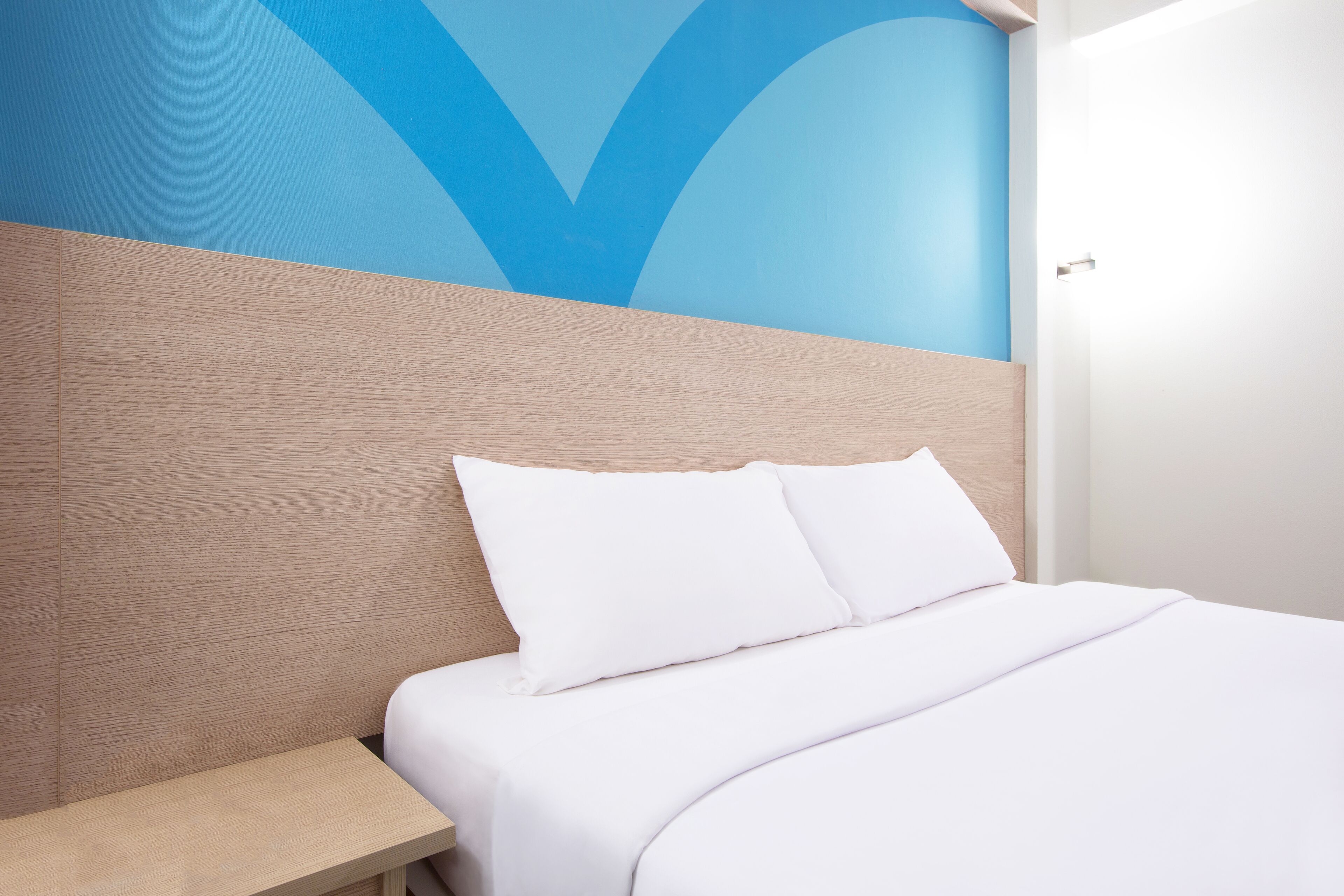 Quarto de hotel com cabeceira de madeira, roupa de cama branca e design de parede azul.