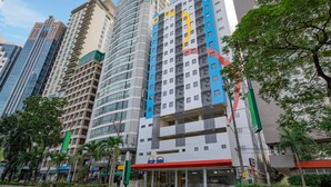 Um hotel de vários andares com design moderno, apresentando um logotipo em destaque na fachada e uma entrada visível.