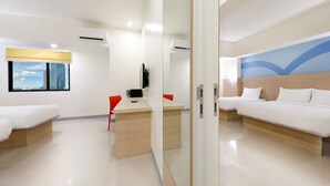 Quarto de hotel moderno com cama, mesas de cabeceira, escrivaninha, poltrona e televisão.