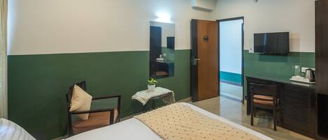 Quarto de hotel com cama, escrivaninha, cadeira, pequena mesa com uma planta, espelho e televisão.