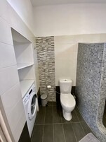 Casa de banho compacta com máquina de lavar roupa, sanita e zona de duche revestida em azulejos.