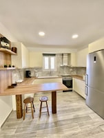 Uma cozinha moderna com bancada de madeira, dois banquetes, uma geladeira de aço inoxidável e uma janela com vista.