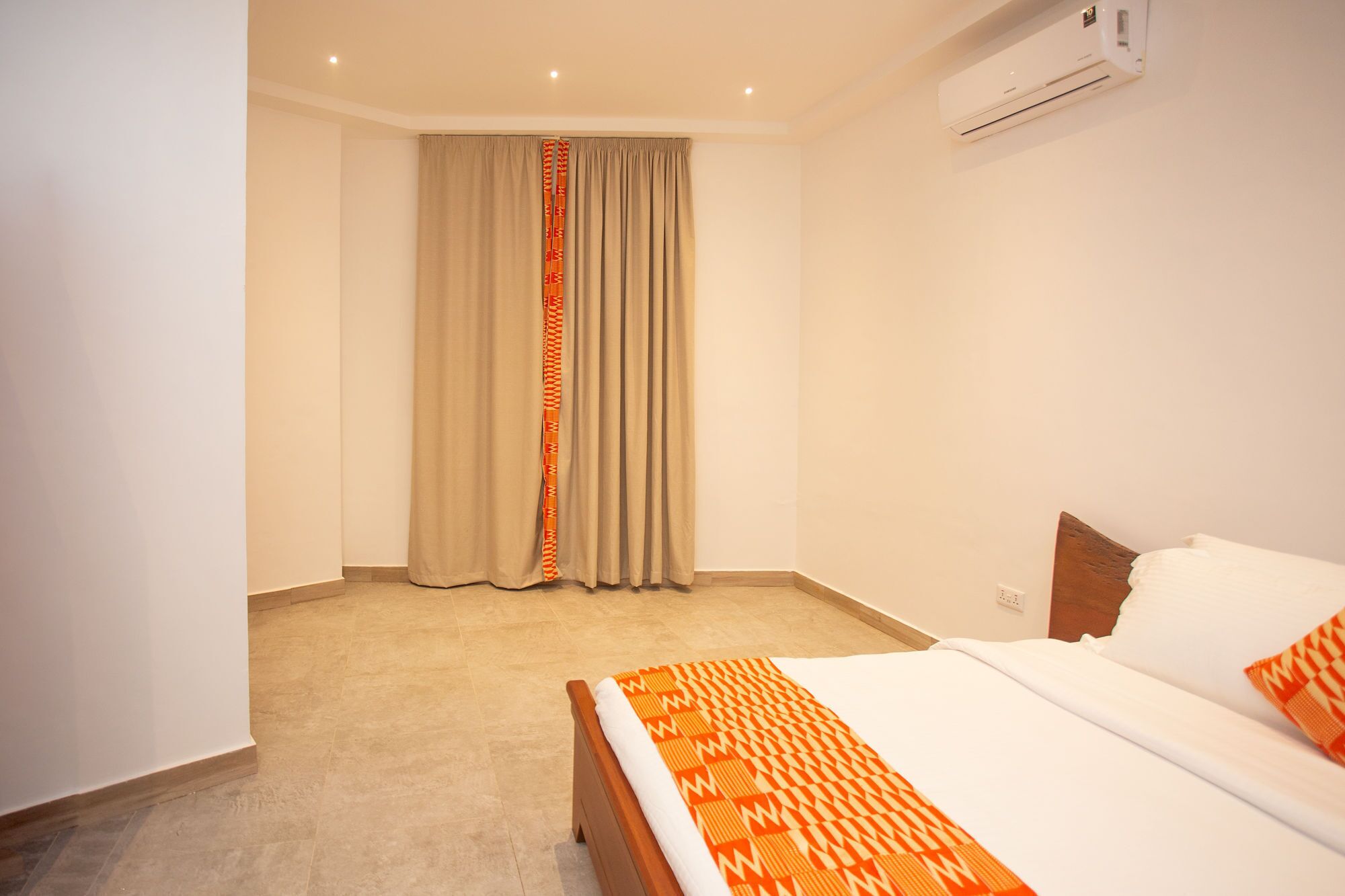 Quarto de hotel com cama, janela com cortinas, ar condicionado e piso coberto por carpete.