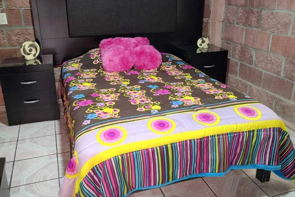 Uma cama com colcha florida e cabeceira, um criado-mudo e uma cômoda.