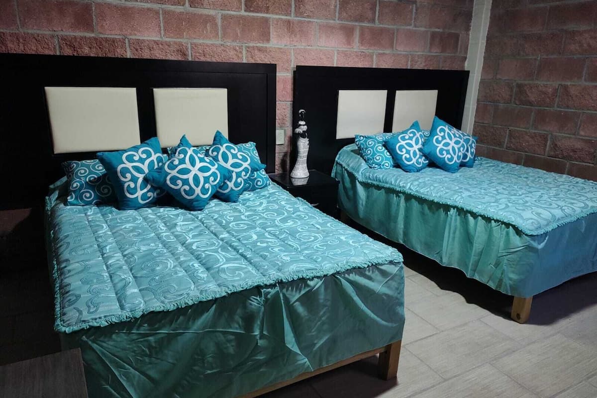 Duas camas de solteiro com roupa de cama azul combinando e almofadas decorativas, apoiadas em uma parede de tijolos.