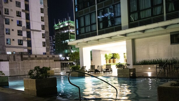 Uma área de piscina à noite, com espreguiçadeiras e um edifício ao fundo.