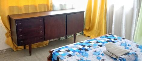 Quarto com cama, cómoda de madeira e janela com cortinas.