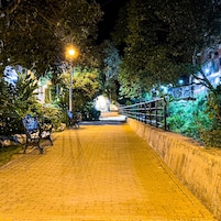 Uma passarela noturna com superfície pavimentada, bancos e corrimão de um lado.