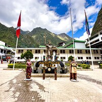 Uma praça com um monumento central, bandeiras e montanhas ao fundo.
