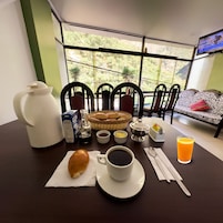 Uma mesa com cadeiras, com louça de café, pão e suco para o pequeno-almoço.
