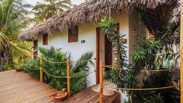 Uma cabana com telhado de palha e deck de madeira, rodeada por plantas tropicais.