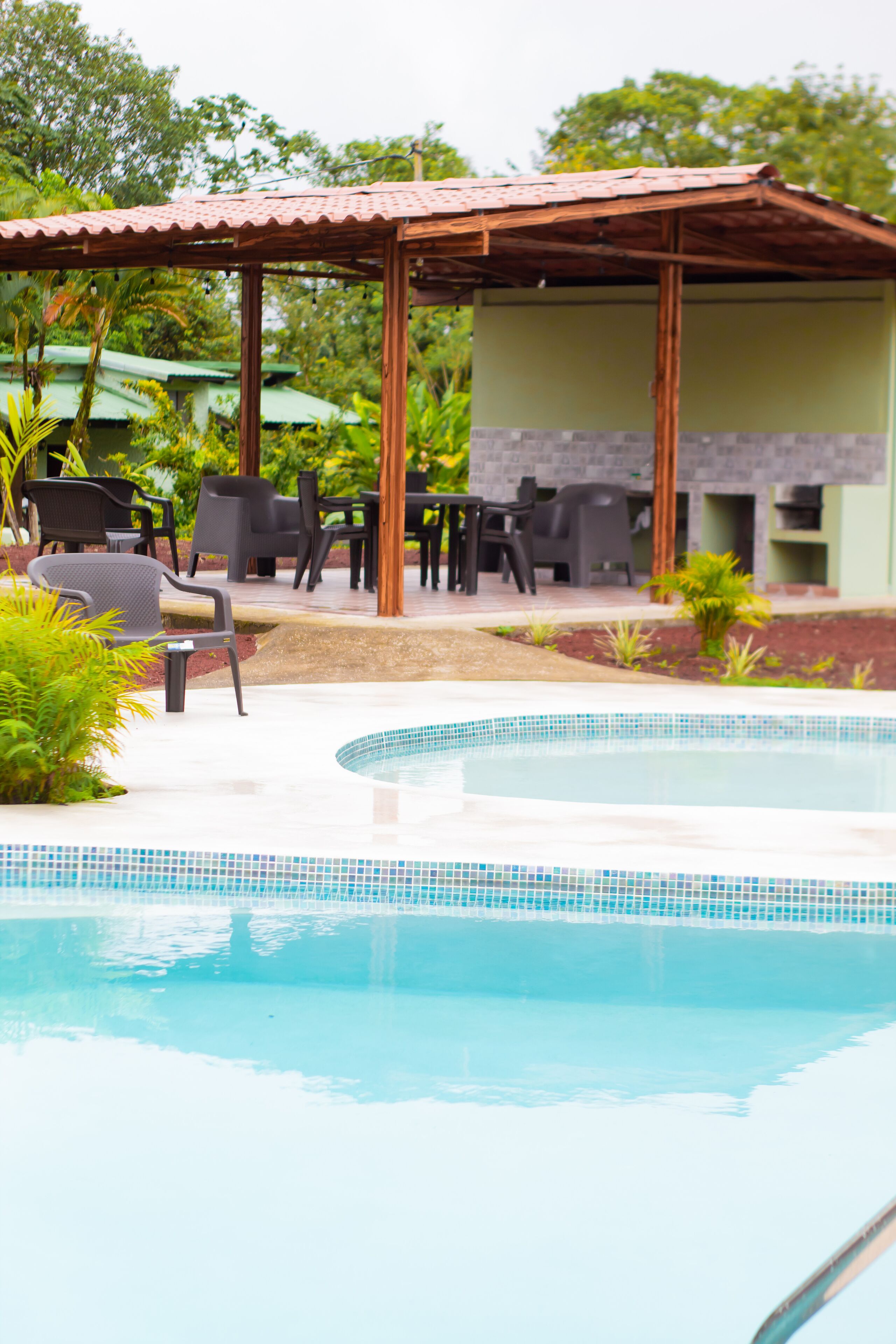 Uma área de piscina com espaço coberto para sentar, espreguiçadeiras e um pequeno jardim.