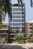 Edifício de vários andares com design arquitetônico moderno, combinando fachadas de vidro e tijolo, e rodeado por vegetação.