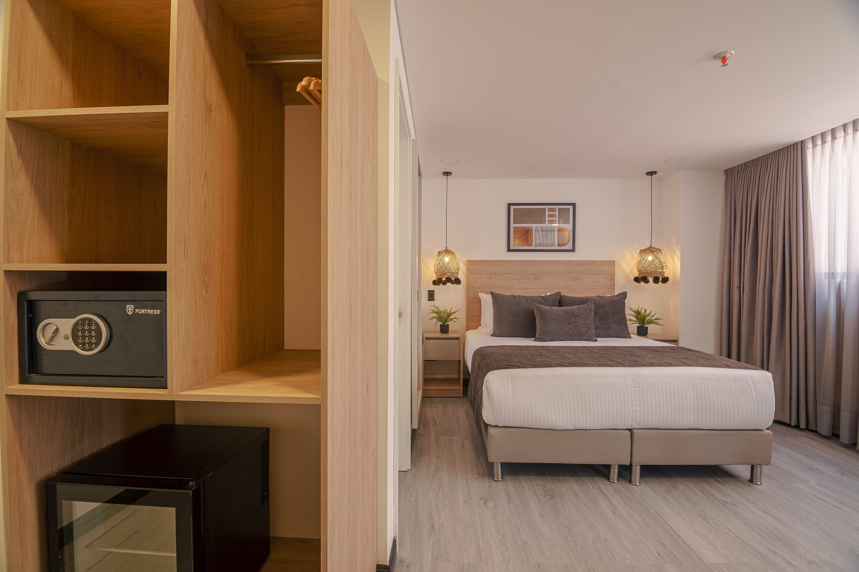Quarto de hotel moderno com uma cama grande, um cofre e um mini-bar.