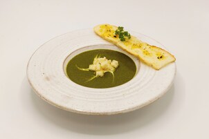 Um prato branco com molho verde, um dente de alho e um pedaço de pão.