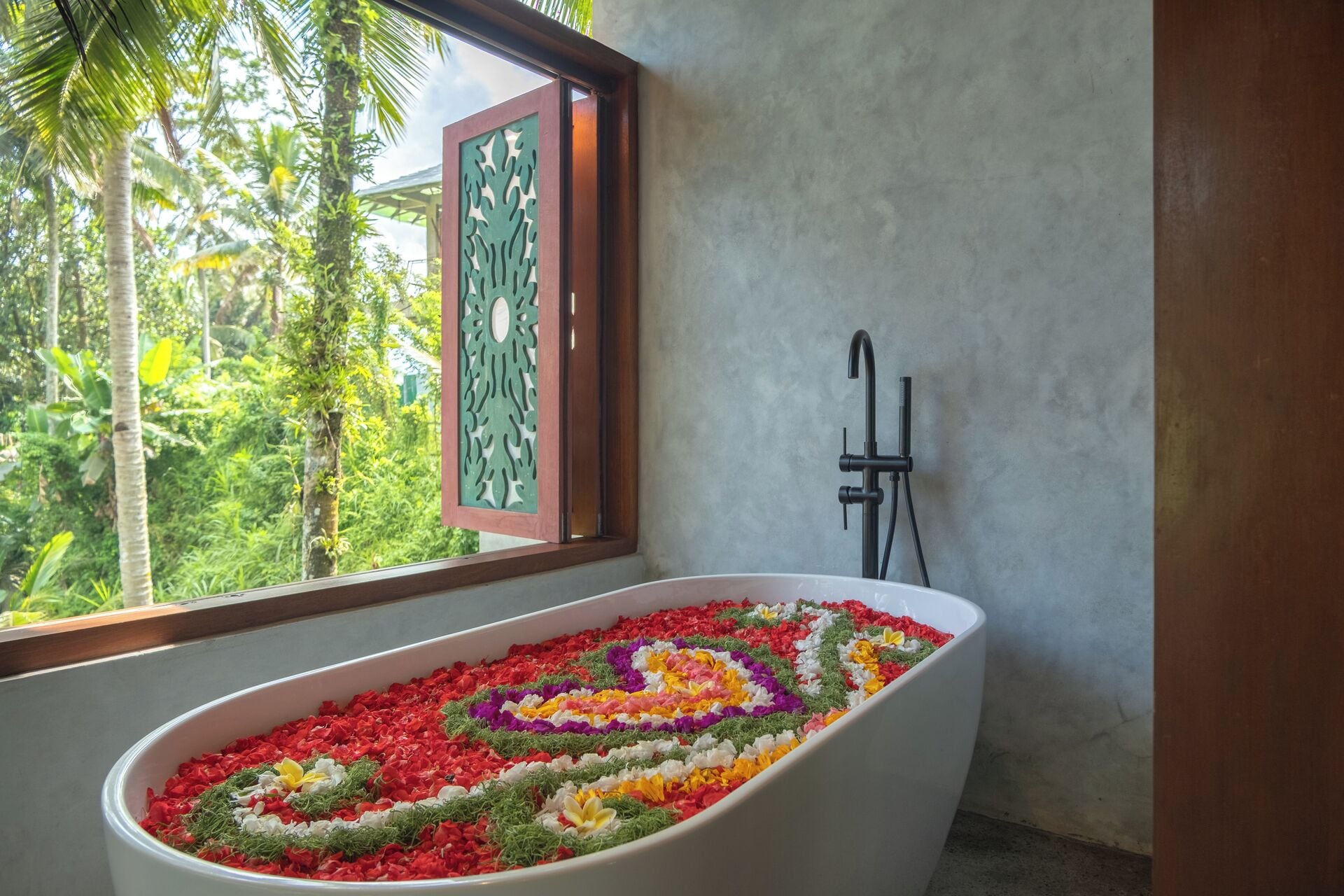 Uma banheira cheia de pétalas de flores coloridas e uma janela com vista para o verde.