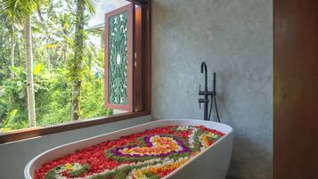 Uma banheira cheia de pétalas de flores coloridas e uma janela com vista para o verde.