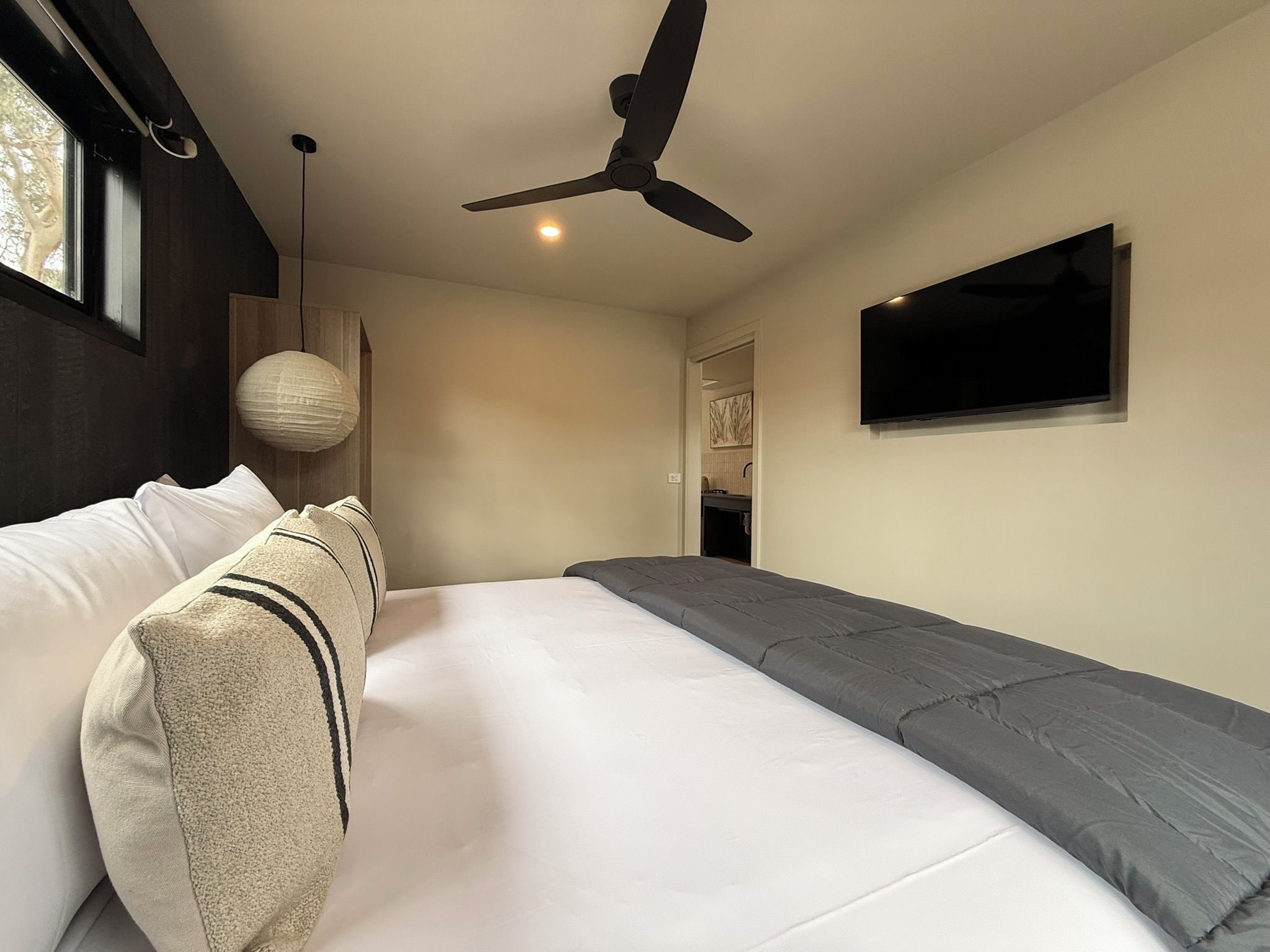 Quarto moderno com cama, ventilador de teto, televisão e janela.