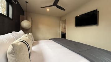 Quarto moderno com cama, ventilador de teto, televisão e janela.