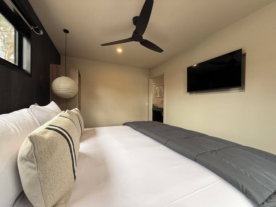 Quarto moderno com cama, ventilador de teto, televisão e janela.