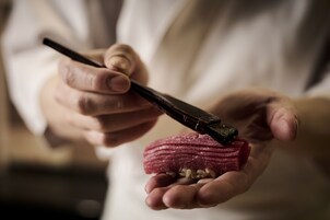 Uma pessoa segurando um objeto rosa pequeno com uma ferramenta, possivelmente um alimento ou um pequeno objeto.