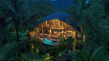 Um edifício em forma de cúpula com piscina, cercado por vegetação tropical.
