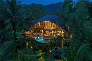 Um edifício em forma de cúpula com piscina, cercado por vegetação tropical.