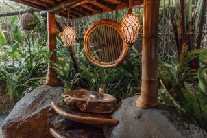 Um ambiente rústico ao ar livre com uma bacia de pedra, estruturas de bambu e lanternas penduradas.