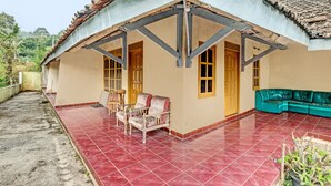 Uma área externa coberta com piso de ladrilho vermelho, móveis de madeira e um sofá verde.