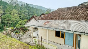Uma casa tradicional com telhado de telhas, rodeada por vegetação exuberante e colinas.
