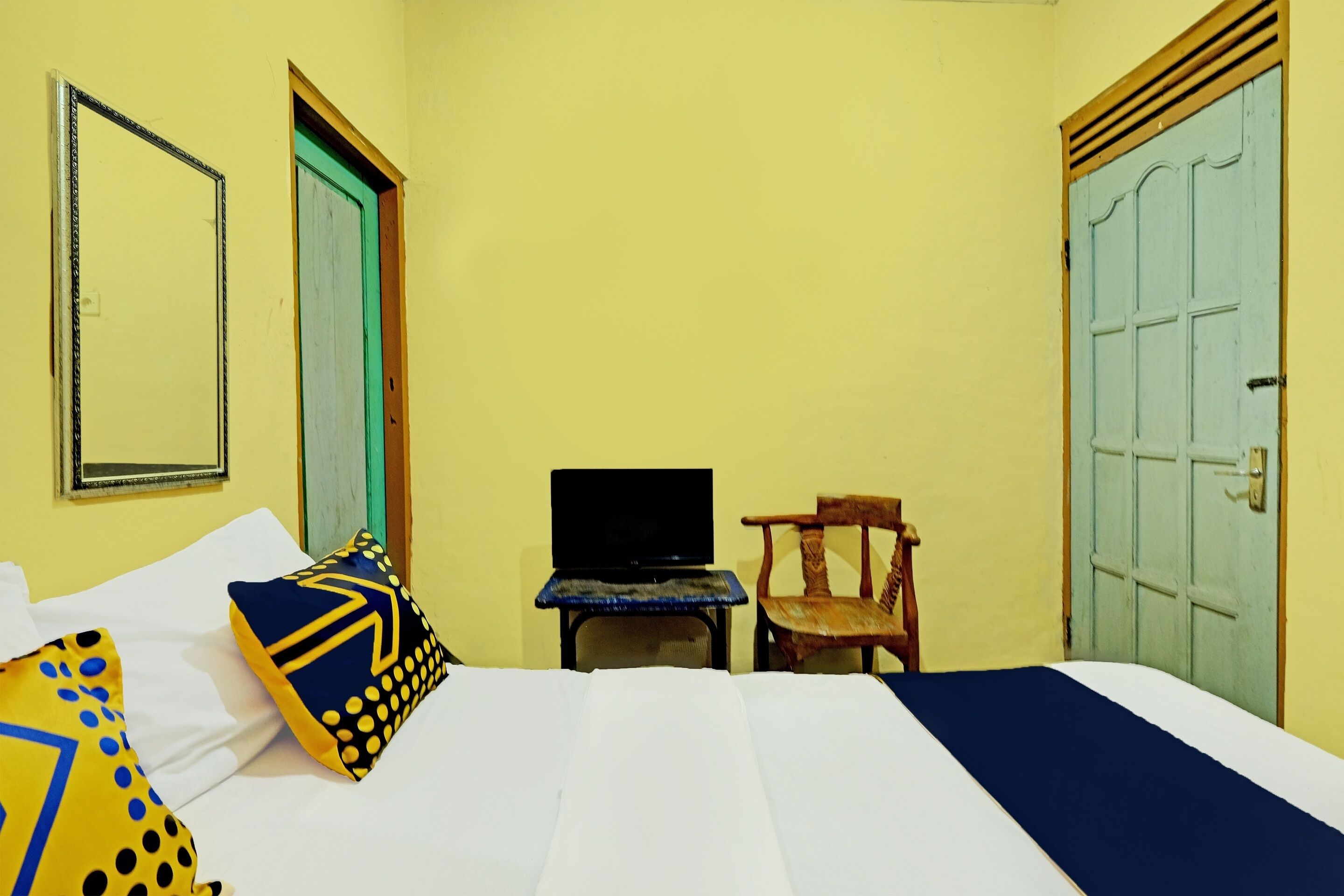 Quarto com uma cama, televisão sobre uma mesinha, uma cadeira e uma porta.