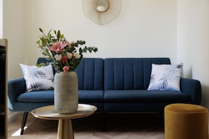 Uma sala de estar moderna com um sofá azul, um vaso estampado com flores e uma mesa redonda.