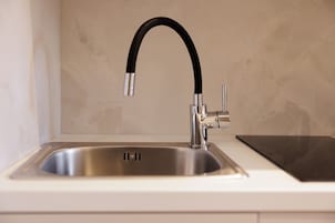 Uma pia de cozinha com uma torneira moderna, uma cuba de aço inoxidável e bancada preta.