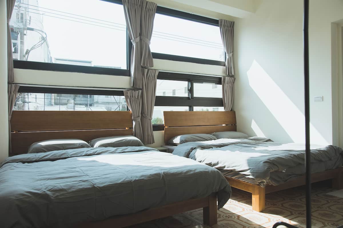 Quarto com duas camas, grandes janelas e vista para a cidade.