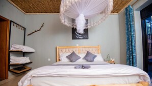Uma cama bem arrumada com cabeceira de madeira, mesa de cabeceira com um frasco e um porta-toalhas fixado na parede.